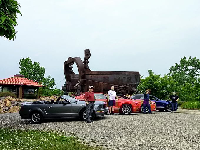 Car enthusiasts gather their prized Mustangs beside the bucket, creating an only-in-America tableau of horsepower meeting industrial power.