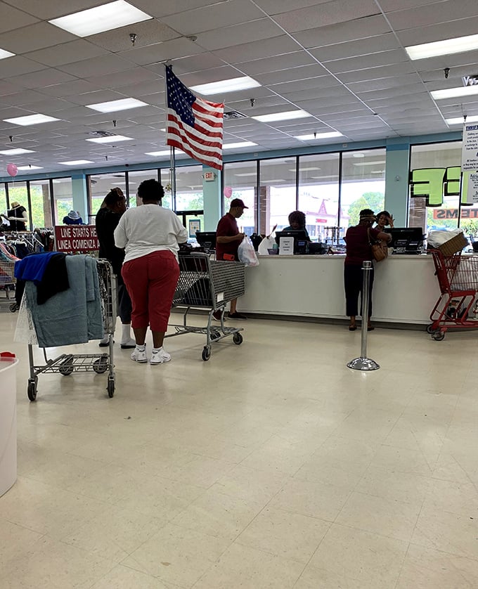 The checkout line: where treasure hunters compare their bounty beneath Old Glory, each cart revealing someone's definition of "essential find."