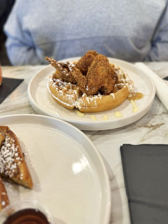 Southern hospitality on a plate: golden fried chicken wings perched atop a waffle throne, dusted with powdered sugar—a sweet and savory alliance that never disappoints.