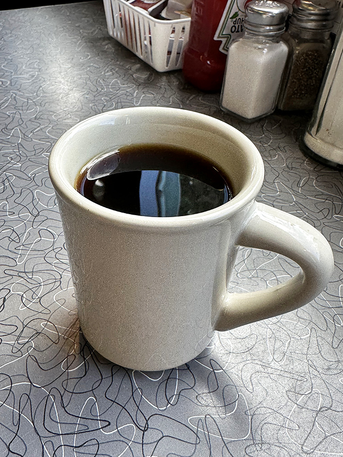 The humble white mug contains the elixir of diner life—strong, honest coffee that doesn't need fancy names or artisanal credentials to get the job done.