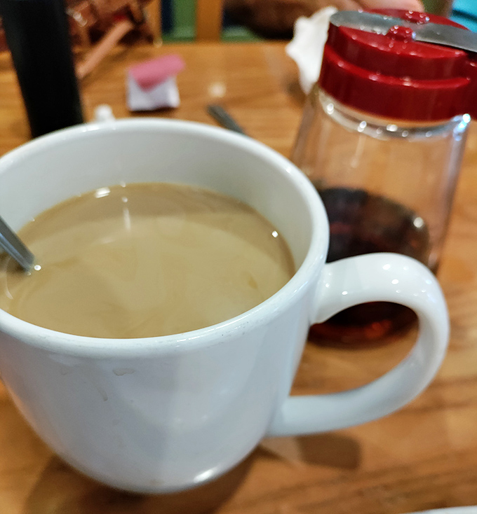 Coffee served in a proper mug—not those dainty cups that leave you wanting. The red sugar dispenser stands ready for those who need the sweet balance.