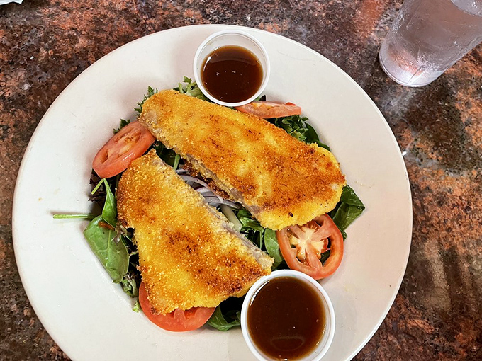 This isn't just fried fish—it's a golden-crusted masterpiece resting on fresh greens with tomatoes, a reminder that simple food done right is culinary poetry.