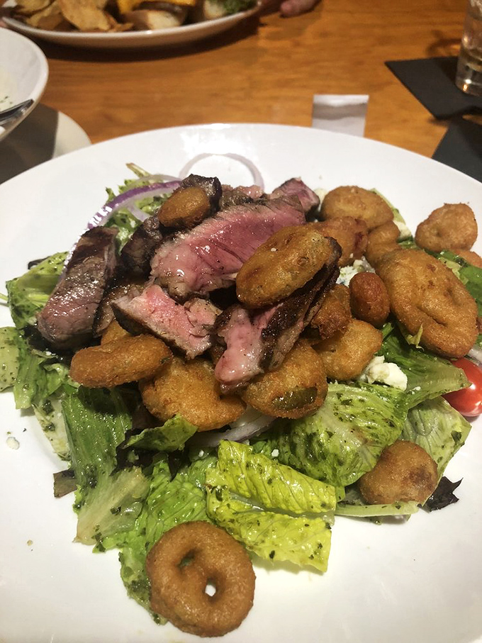 Steak salad that solves the eternal dilemma: "I should eat healthy, but I want steak." Those crispy onion rings aren't garnish—they're little halos of happiness. 
