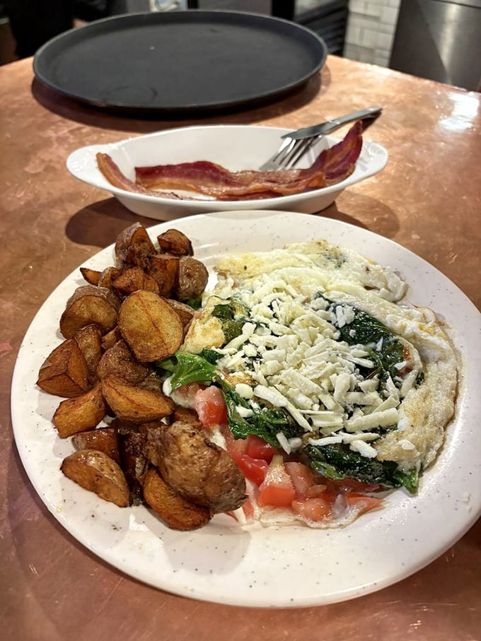 The Greek Omelette arrives like a Mediterranean vacation on a plate—spinach, tomatoes, and feta cheese creating a breakfast United Nations.