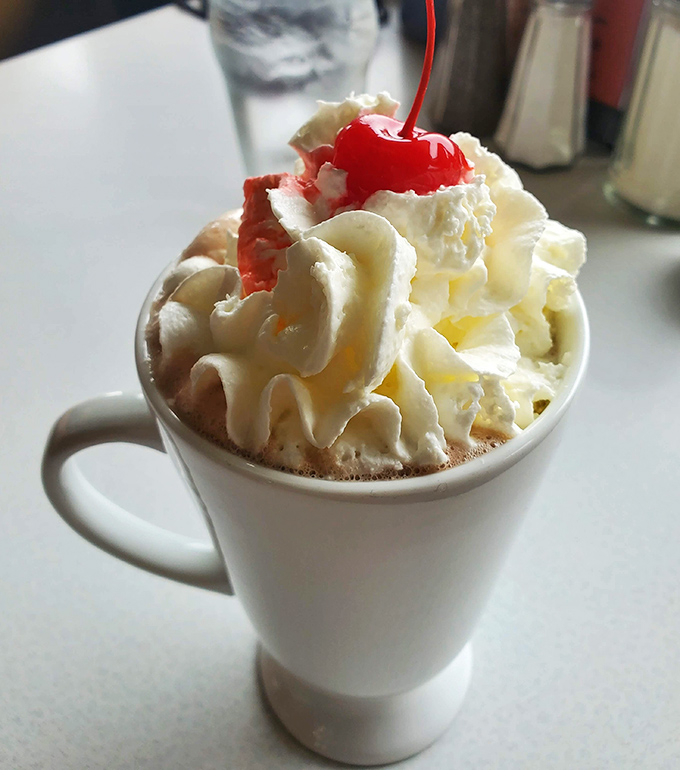 Hot chocolate elevated to an art form—whipped cream mountain, cherry on top, and somewhere beneath it all, liquid happiness waiting to be sipped.