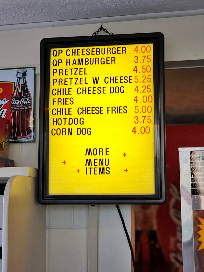The illuminated yellow menu board showcases drive-in classics like cheeseburgers and corn dogs. Simple pleasures at reasonable prices—a refreshing concept!