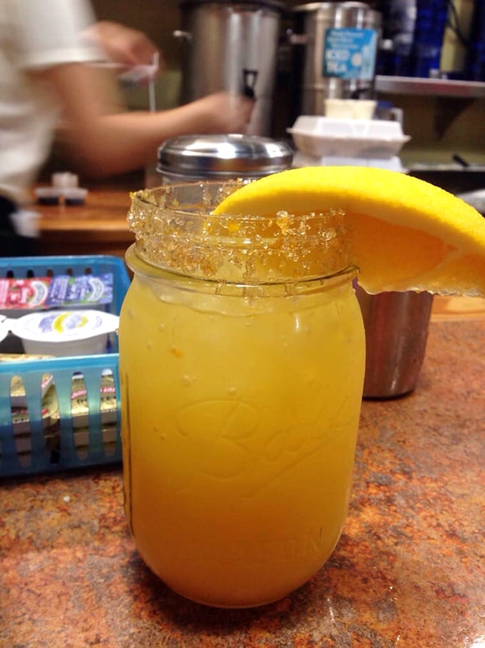 A mason jar mimosa with a sugar rim and orange slice that says, "Yes, it's technically morning, but we're in Florida and life is good."