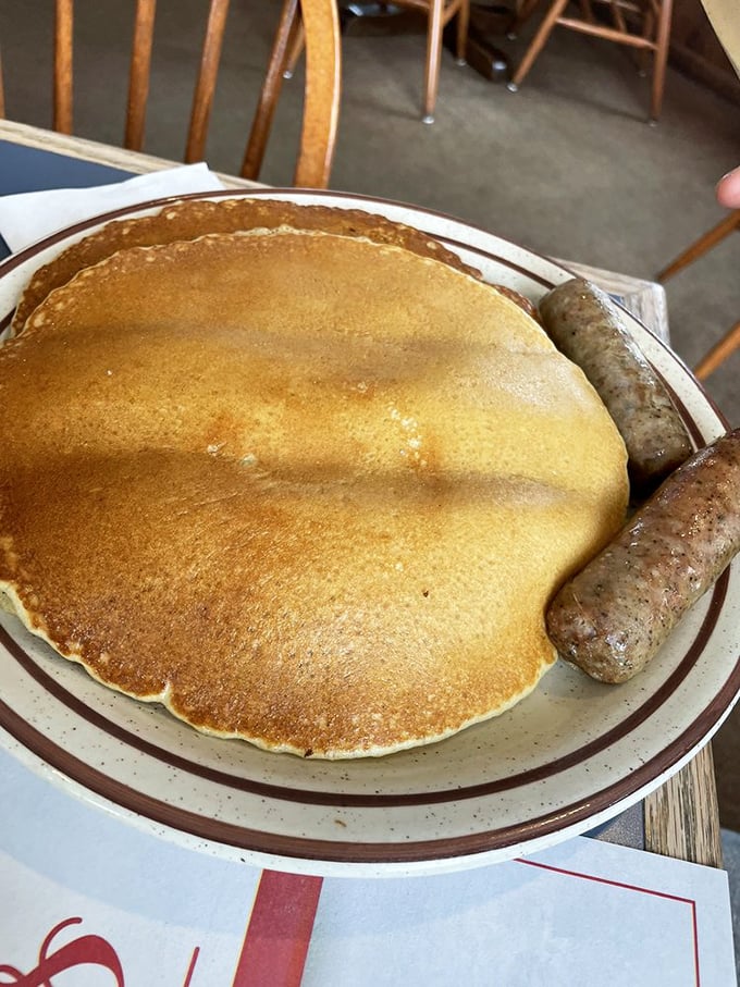 This pancake is living its best life – golden, enormous, and hanging out with sausage links that clearly graduated from the same culinary school of excellence.