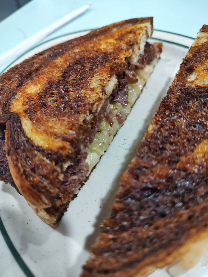 The patty melt—that brilliant marriage of burger and grilled cheese—toasted to the exact shade of brown that triggers immediate salivation.