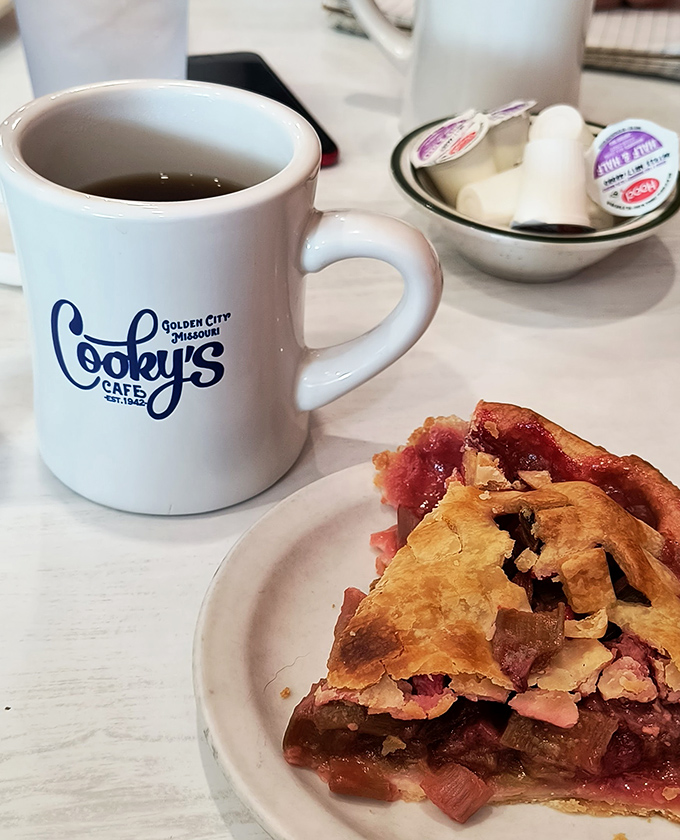 A slice of strawberry-rhubarb alongside Cooky's signature mug—proof that sometimes the simplest combinations create the most profound happiness.