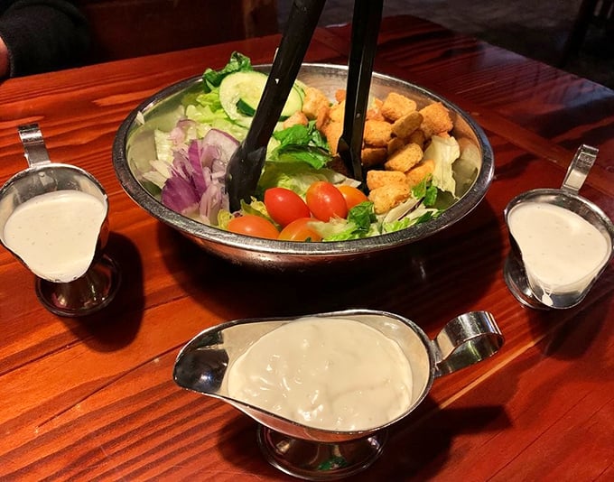 Even the salad gets the royal treatment—a metal mixing bowl of fresh greens with dressing options served in silver gravy boats, because ranch deserves respect too.