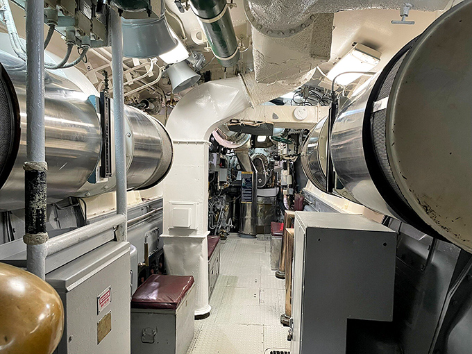 Massive pipes, valves, and machinery line this passageway. Every inch of submarine real estate served a purpose – form following function with military precision.