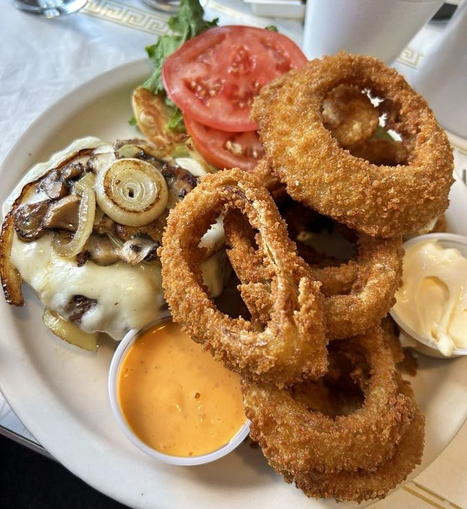 Onion rings stacked like golden halos around a burger that's been kissed by the flat-top gods. The side of cheese sauce isn't optional—it's essential.