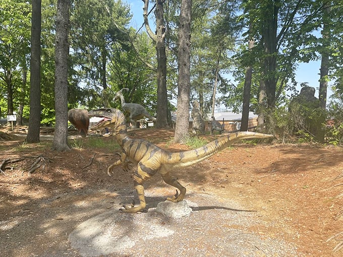 The path winds through a prehistoric forest where raptors lurk among the trees, their hunting postures frozen in mid-stalk.