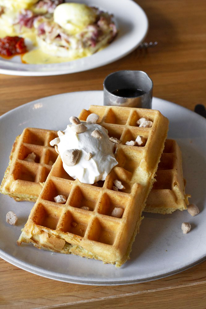 Golden waffles crowned with whipped cream and tiny crunchies—breakfast that makes you wonder why we don't eat dessert first every day.