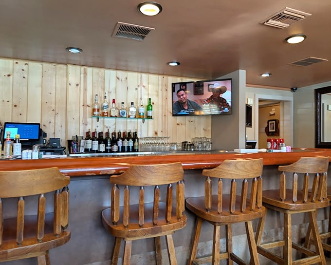 The bar at D'Carlos—where wooden stools await, spirits stand at attention, and the TV ensures you won't miss the game while savoring your pre-dinner Old Fashioned.