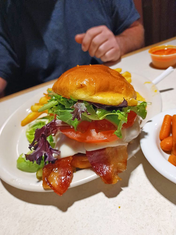 A burger built like a skyscraper of flavor—bacon, cheese, fresh vegetables, and a bun that somehow manages to contain this beautiful chaos.