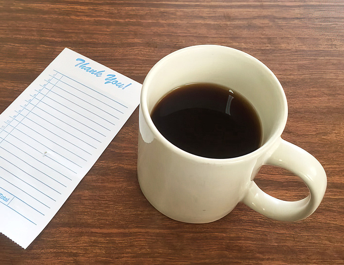 Simple white mug, black coffee, checkered receipt pad—the holy trinity of diner breakfast. No fancy latte art needed when the coffee itself tells the story.