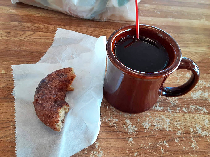 The classic pairing: strong coffee in a sturdy mug alongside a half-eaten donut – evidence of someone with proper life priorities.
