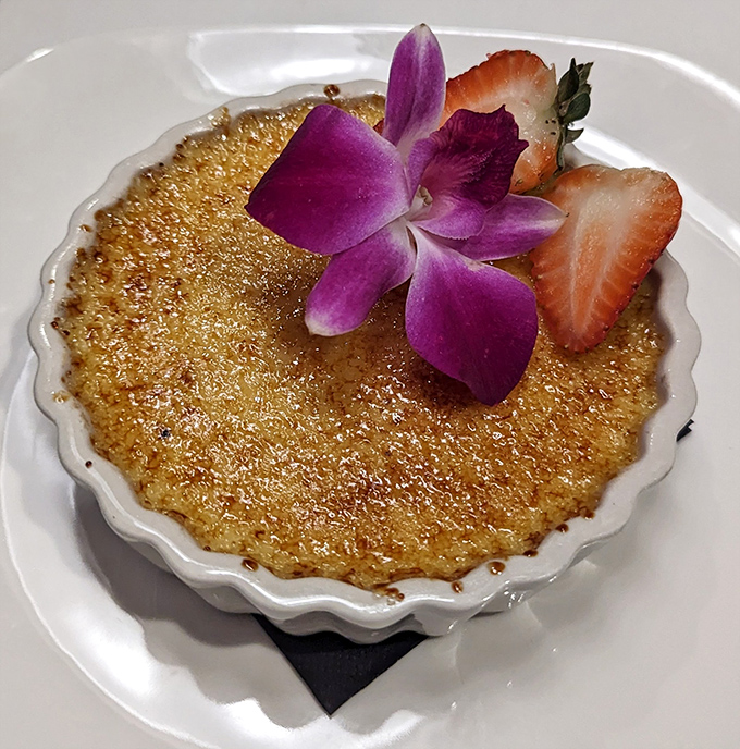 The crème brûlée's crackling sugar top gives way to silky custard beneath—a textural tango that never disappoints, especially with that edible purple flower garnish.