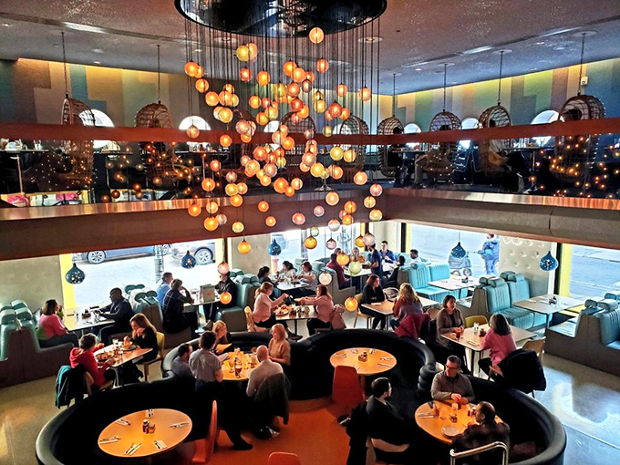 The dining room buzzes with energy as the spectacular hanging light installation creates a galaxy of warm glowing orbs above happy diners.