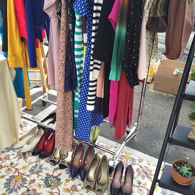 A rainbow of dresses dangles above a carefully arranged shoe collection—the flea market equivalent of a walk-in closet that spans several decades of style.