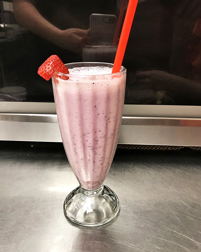 A strawberry shake that bridges the gap between childhood nostalgia and grown-up indulgence. That fresh berry garnish isn't fooling anyone—this is dessert masquerading as a beverage.