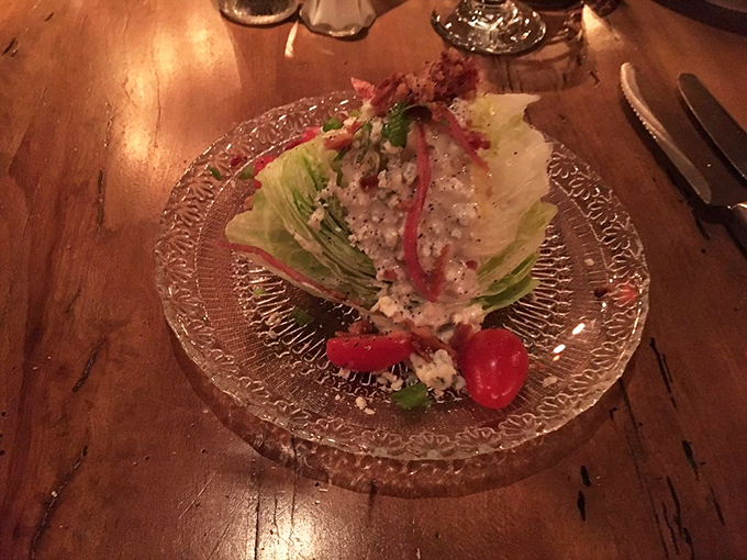 The wedge salad—that steakhouse classic—gets the royal treatment with blue cheese crumbles and cherry tomatoes on a plate fancy enough for the occasion.