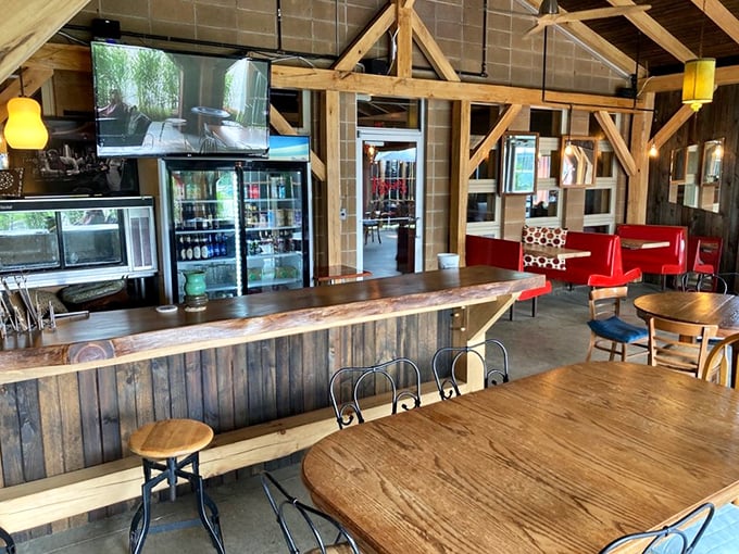 The bar area blends rustic charm with modern comfort – wooden beams overhead, live-edge bar top, and those inviting red booths calling your name.