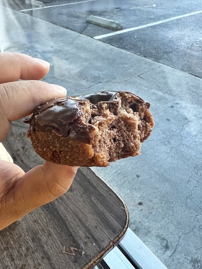 Half-eaten chocolate cake donut reveals its dense, moist interior—proof that sometimes the best food photography happens mid-bite.