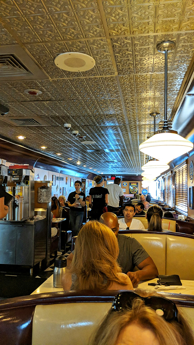 The bustling interior reveals the diner's heartbeat—servers weaving between booths, delivering plates of happiness under those classic pressed tin ceilings.