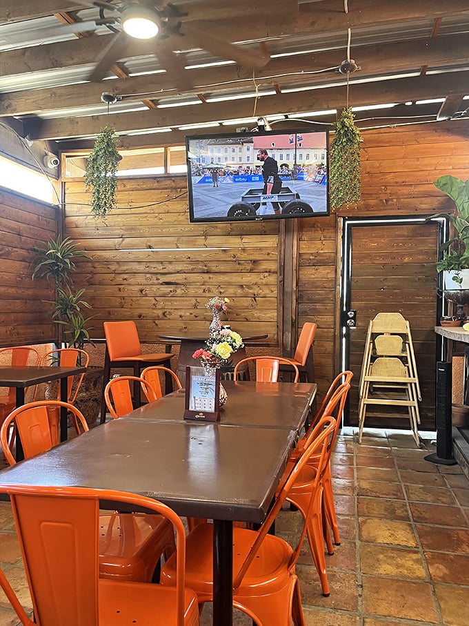 Orange metal chairs add a pop of modern flair to the rustic wooden dining area, where televisions and hanging plants create a homey vibe.