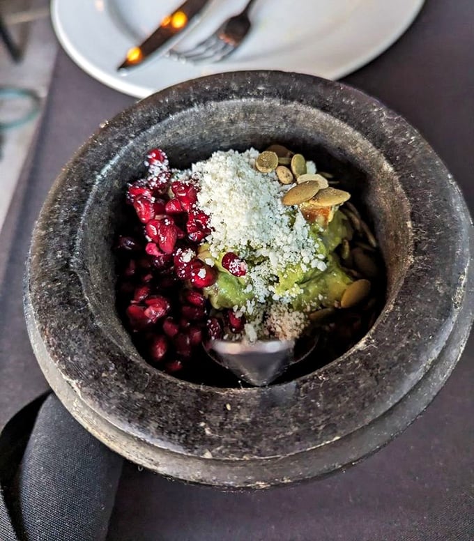 A stone molcajete cradles the holy trinity of Mexican flavors—pomegranate jewels, creamy avocado, and pepitas—ready for your chip-dipping pleasure.