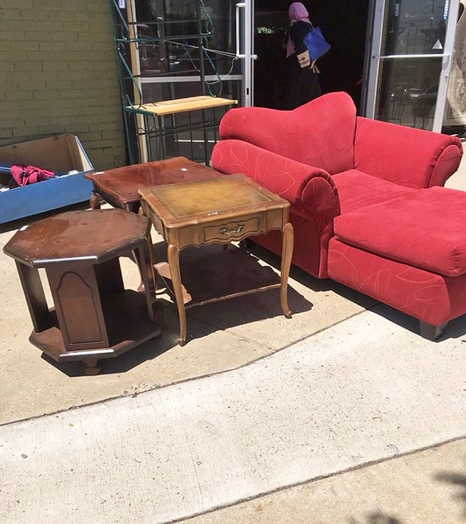 The sidewalk showcase—where furniture gets a sunbath while waiting for its forever home. That red loveseat is practically waving at passersby.