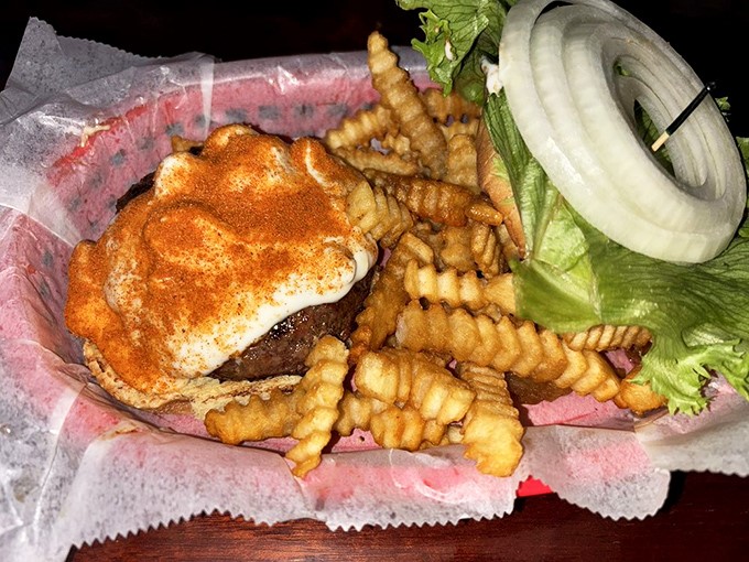 A burger that bites back. The spicy blue cheese creation sits proudly on its throne of crinkle-cut fries, daring you to take the first bite.