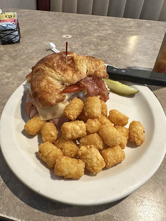Not all heroes wear capes, but this croissant sandwich—stacked with turkey and accompanied by golden tater tots—definitely saves the day.