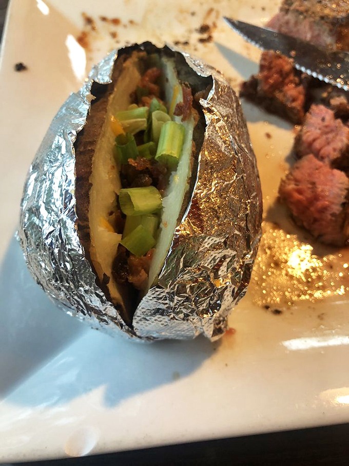 Not just any baked potato—this foil-wrapped treasure comes loaded with green onions, ready to play the perfect supporting role to your steak.