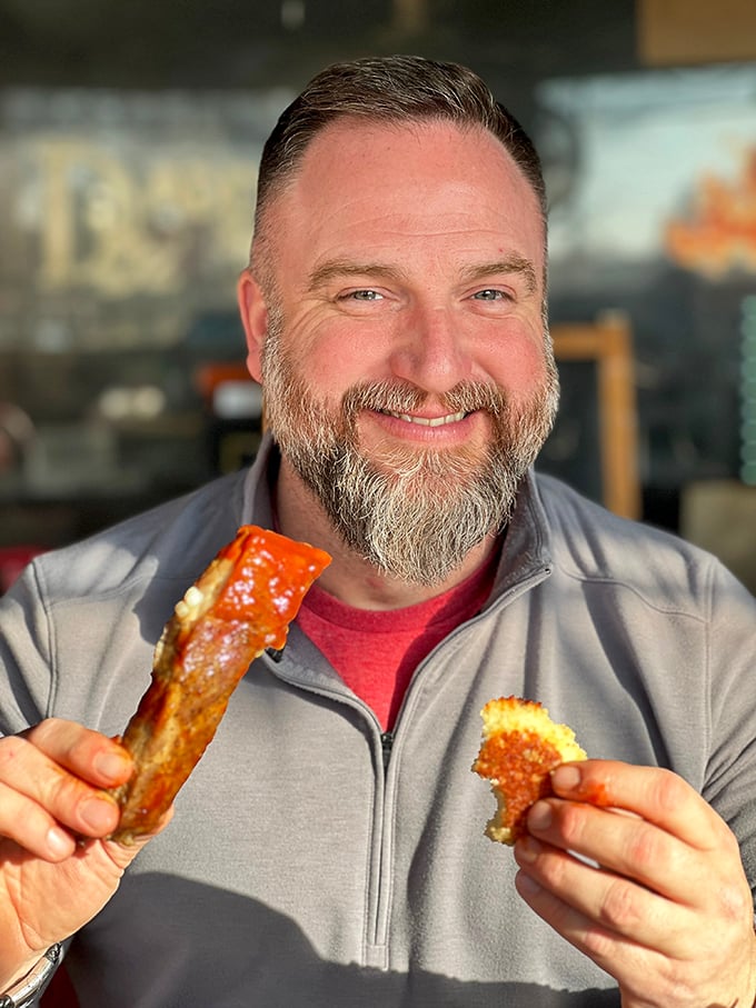 The image shows a smiling patron enjoying what appears to be barbecue delights—the universal expression of someone who's found their happy place.