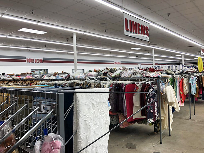 Under the "LINENS" sign, bedsheets and tablecloths hang like textile ghosts of domestic life, ready to be reincarnated in new homes.