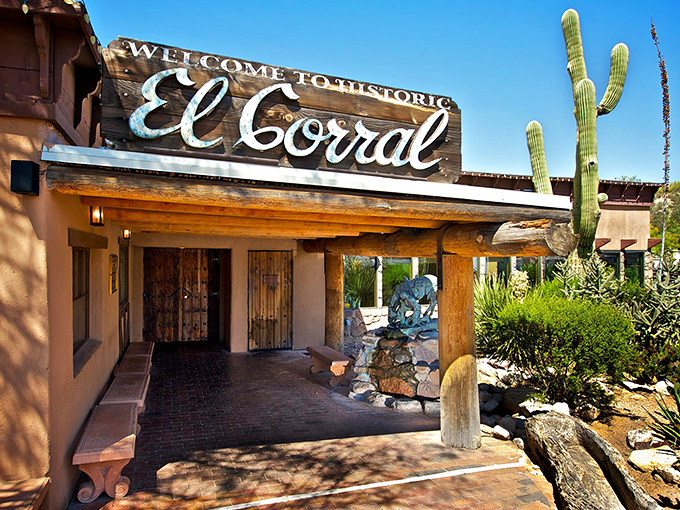 The iconic entrance to El Corral welcomes diners with rustic Southwestern charm, saguaro sentinels, and the promise of mesquite-grilled perfection.
