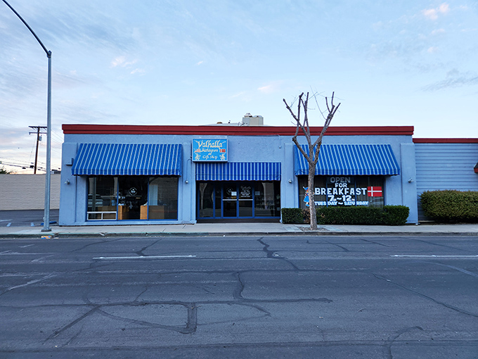 The unassuming entrance to Valhalla beckons with its simple blue sign and cheerful yellow flowers – proof that culinary paradise doesn't always need a flashy entrance.