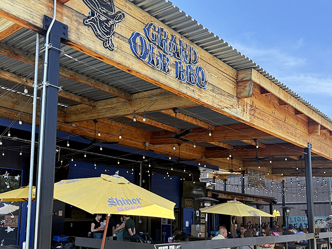 The rustic wooden facade of Grand Ole BBQ beckons like a smoke signal to barbecue pilgrims. Those yellow umbrellas aren't just for show—they're holding space for your BBQ dreams.