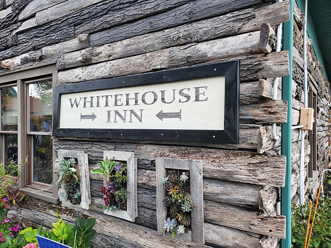 The weathered log cabin exterior of The Whitehouse Inn beckons like a rustic time machine, promising comfort food treasures behind that unassuming wooden facade.