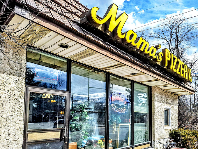 The iconic yellow sign of Mama's Pizzeria stands out against cherry blossoms like a culinary landmark that locals have treasured for generations.