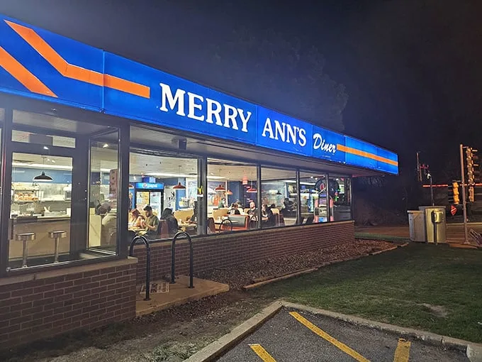 The blue and orange beacon of Merry Ann's Diner glows like a lighthouse for the hungry, promising comfort food salvation at any hour of the night.