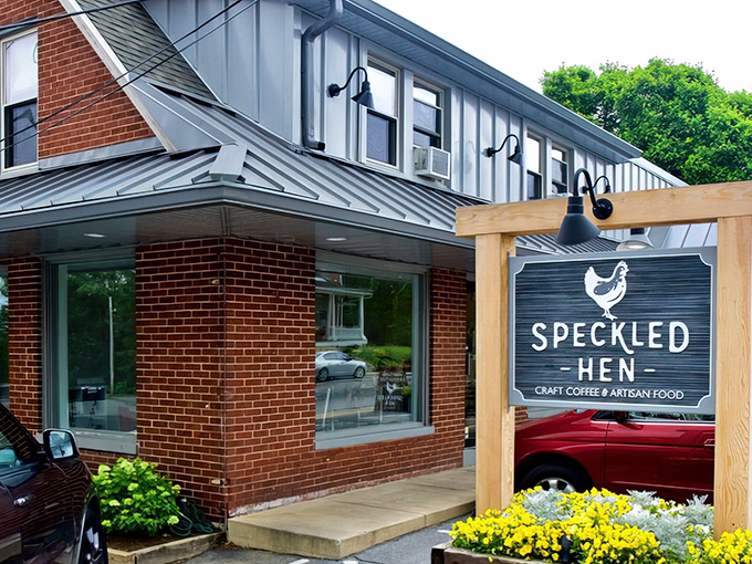 The welcoming wooden sign for Speckled Hen stands proudly amid vibrant flowers, promising craft coffee and artisan food in Strasburg's charming downtown setting.