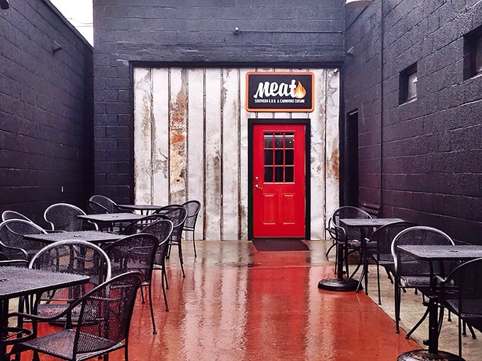 That bright red door between black walls isn't just an entrance—it's a portal to barbecue nirvana. The outdoor seating area beckons with the promise of smoky delights.