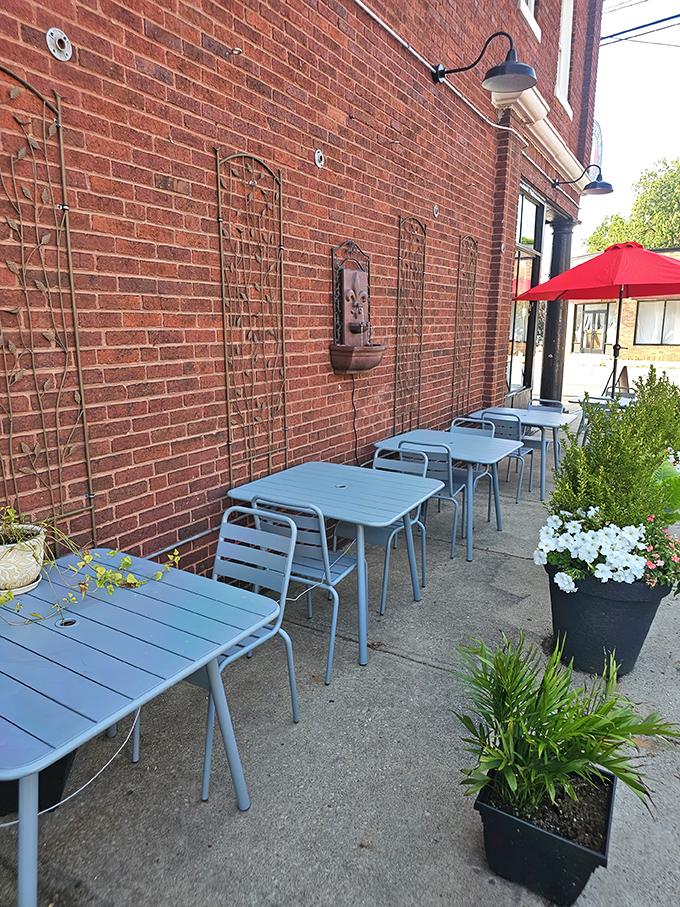 The exposed brick exterior of Peppers Italian Restaurant sets the stage for a cozy outdoor dining area, featuring light blue tables, lush greenery, and a bold red umbrella—all perfect for enjoying fantastic food without the fuss.