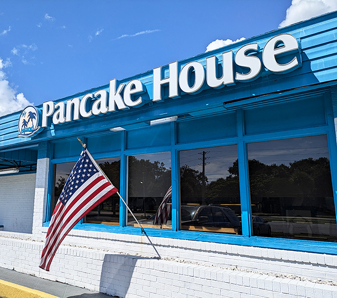 The cheerful blue facade of My Island Pancake House stands proudly against Florida's sky, American flag waving a warm welcome to hungry visitors.
