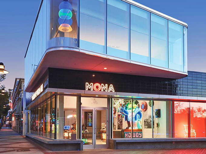 MONA's striking glass façade transforms from museum by day to glowing art installation by night, beckoning curious passersby into its luminous world.